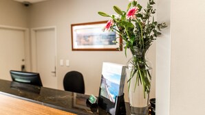 Uma receção com um vaso de flores, um quadro emoldurado e um expositor de folhetos.