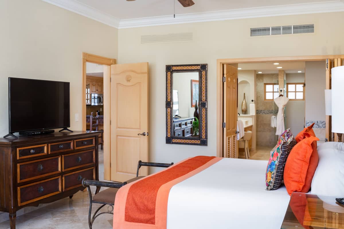 Quarto de hotel com cama, televisão, cômoda e banheiro visível por uma porta aberta.