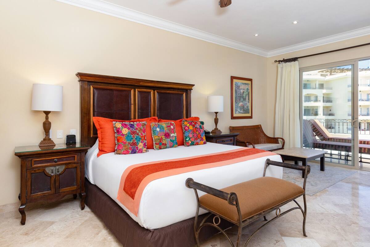 Quarto de hotel com uma cama grande, duas mesas de cabeceira, uma cadeira e varanda com vista para o edifício.