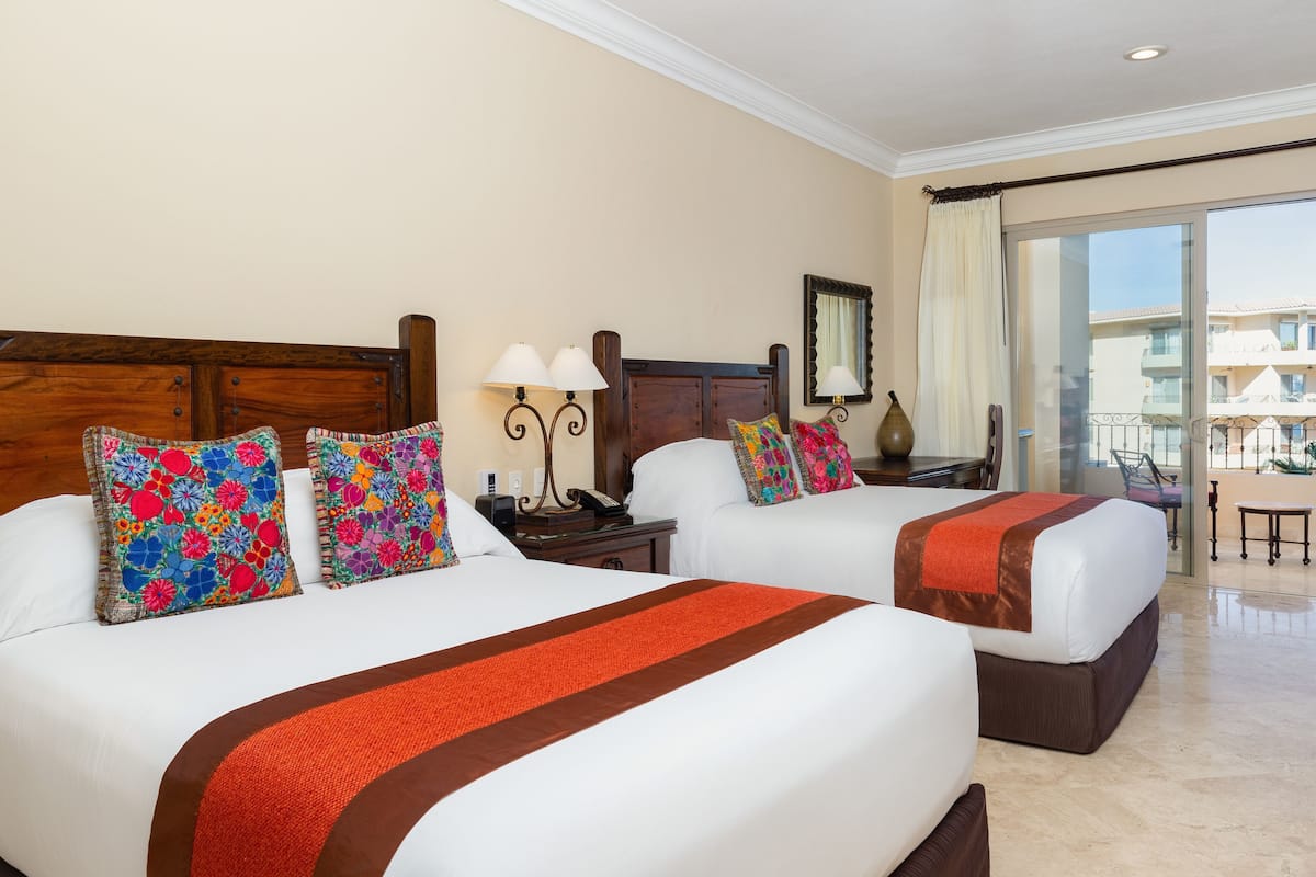 Quarto de hotel com duas camas, uma mesa de cabeceira com abajur, um espelho e vista para a varanda.