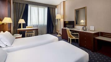 Quarto de hotel com duas camas, uma mesa, uma cadeira, televisão e espelho.