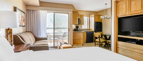 Quarto de hotel com cama grande, sofá, mesa de jantar e cozinha.