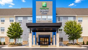 Edifício da Holiday Inn Express & Suites com fachada azul e bege, entrada central com toldo e duas árvores em primeiro plano.