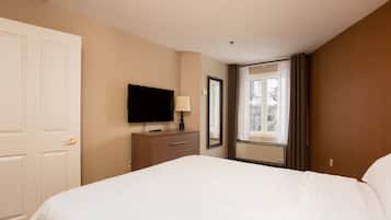 Quarto de hotel com uma cama, televisão sobre uma cômoda, janela com cortinas e uma porta.