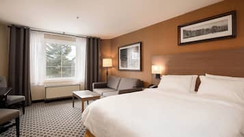 Quarto de hotel com uma cama grande, uma escrivaninha, uma cadeira, um abajur e um quadro na parede.
