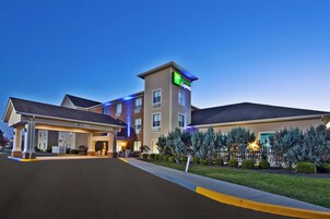 Um hotel Holiday Inn Express com entrada acessível, estacionamento e um gramado bem cuidado com árvores perenes.