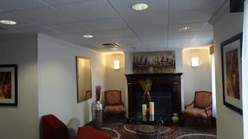 Um quarto com lareira, duas poltronas, uma mesa com velas e um espelho grande.