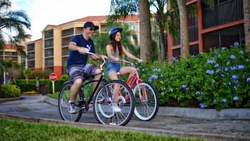 Duas pessoas de bicicleta numa calçada, com uma placa de pare e um edifício ao fundo.
