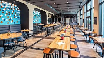 Restaurante moderno com mesas comunitárias alongadas e cabines, apresentando uma parede com padrão geométrico e amplas janelas.