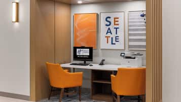 Quarto de hotel com escrivaninha, duas cadeiras laranja, computador e impressora.