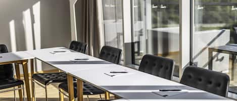 Uma sala de conferências com uma mesa comprida, cadeiras pretas e vista para o exterior através de grandes janelas.