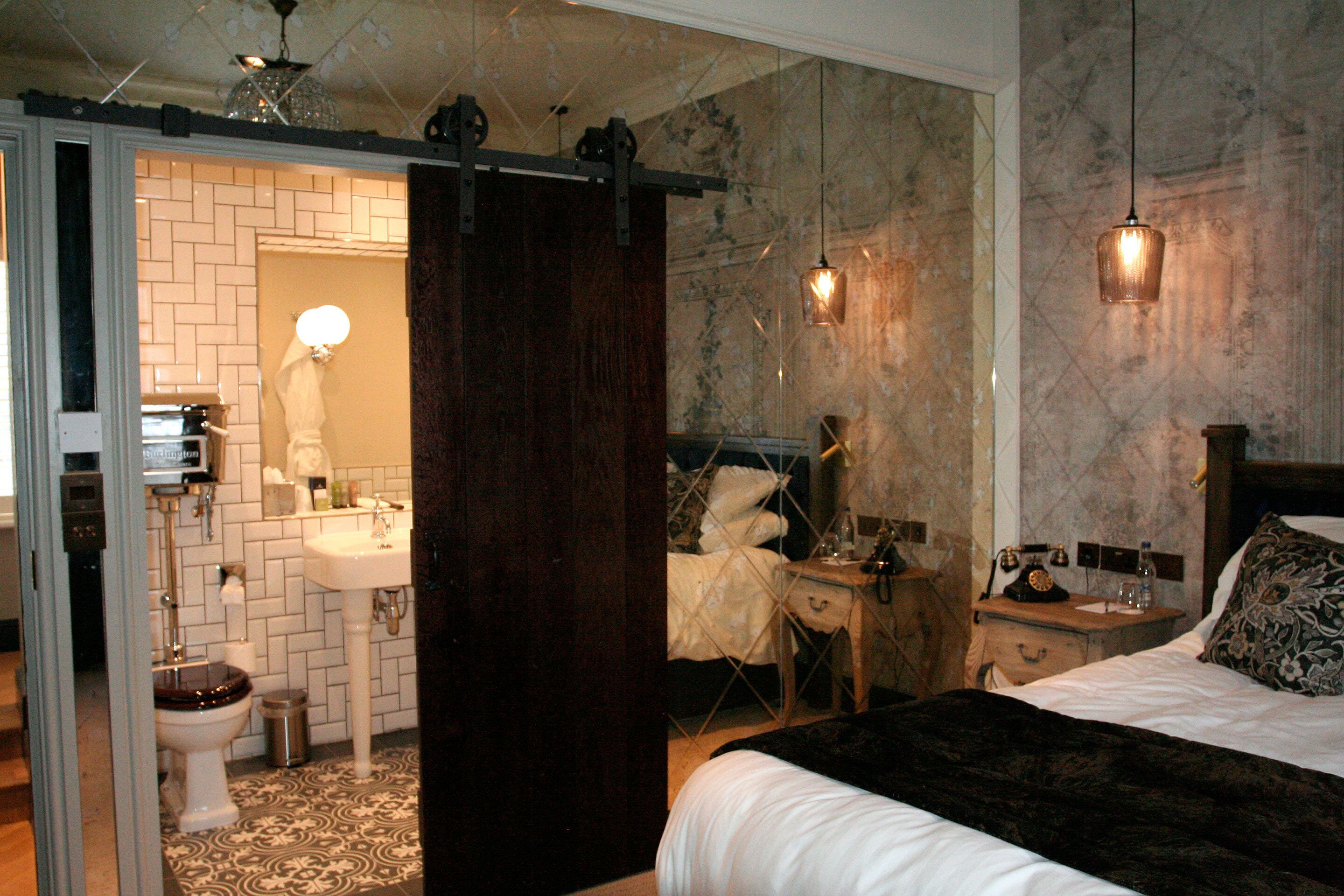 Quarto com cama, mesa de cabeceira, penteadeira, espelho e banheiro com vaso sanitário e pia.