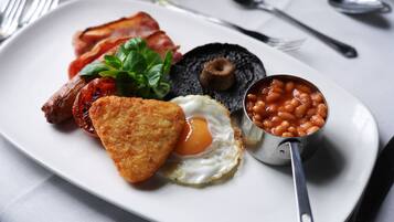 Um prato de comida para o pequeno-almoço, incluindo bacon, ovos, feijão e cogumelos.