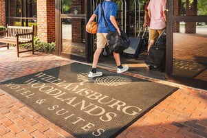 Entrada de hotel com um tapete de entrada com a inscrição 'WILMINGTON HOODLANDS SUITES' e um banco à esquerda.