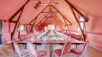 Uma sala de conferências com uma mesa comprida, cadeiras vermelhas e um teto alto com vigas de madeira.