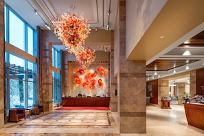 Um saguão de hotel com uma grande escultura de vidro, uma recepção e uma área de estar.
