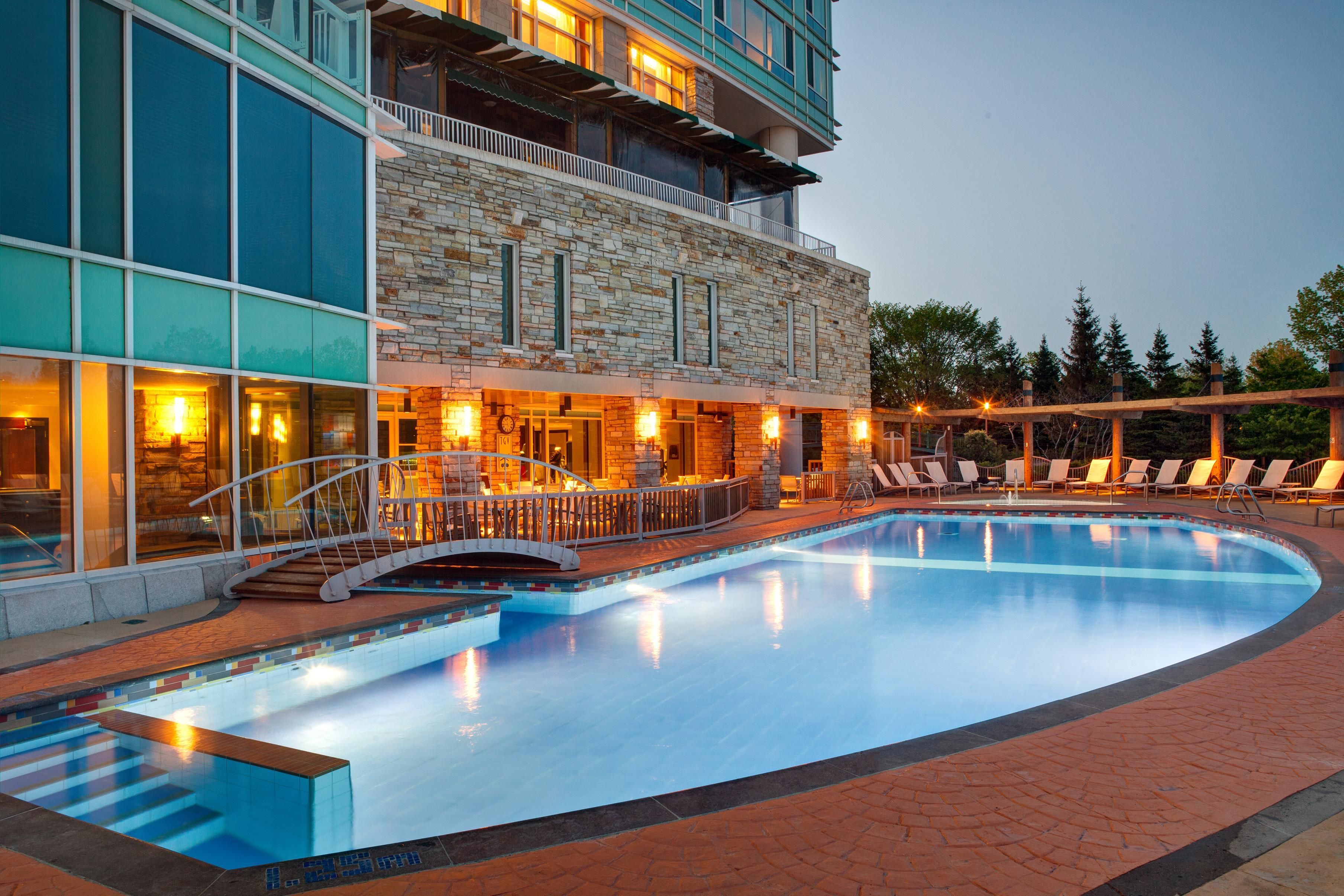 Hotel com piscina, fachada de pedra e área coberta com espreguiçadeiras.