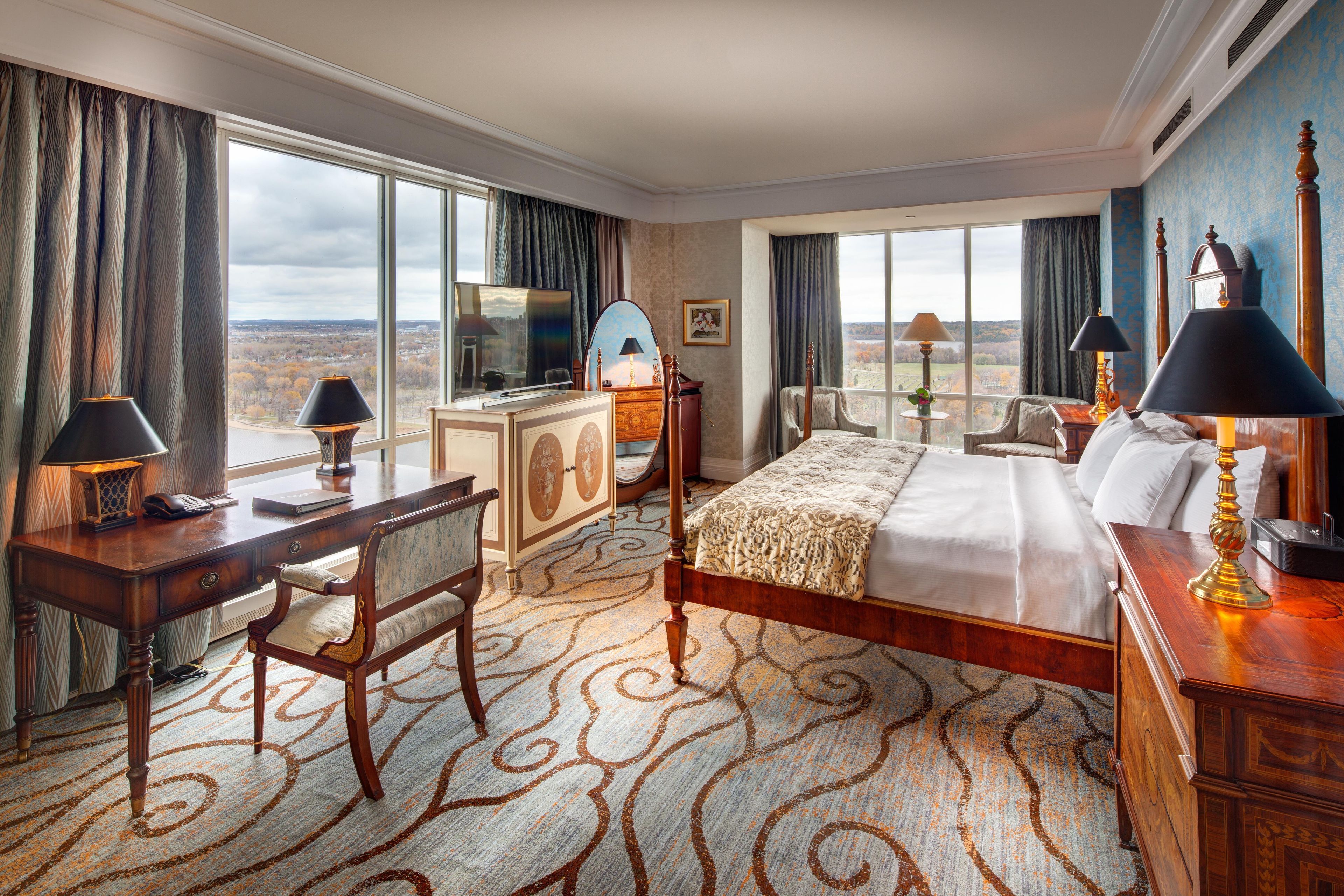 Quarto de hotel com uma cama grande, escrivaninha, cadeira, cômoda e vista para a paisagem.
