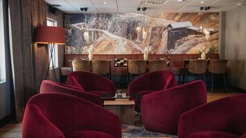 Restaurante com cadeiras estofadas vermelhas, um mural grande de uma estrada de montanha e iluminação pendente.