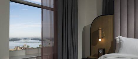 Quarto de hotel com uma janela ampla que dá para uma ponte e para a água.