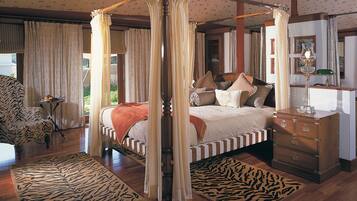Uma cama de dossel com colunas, cabeceira de madeira, tapete com padrão de zebra, mesa de cabeceira de madeira e abajur verde.