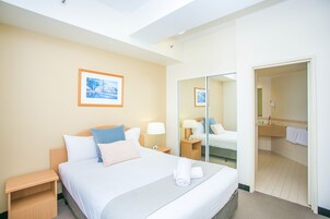 Quarto de hotel com cama, mesas de cabeceira, um espelho e um banheiro visível através de uma porta aberta.