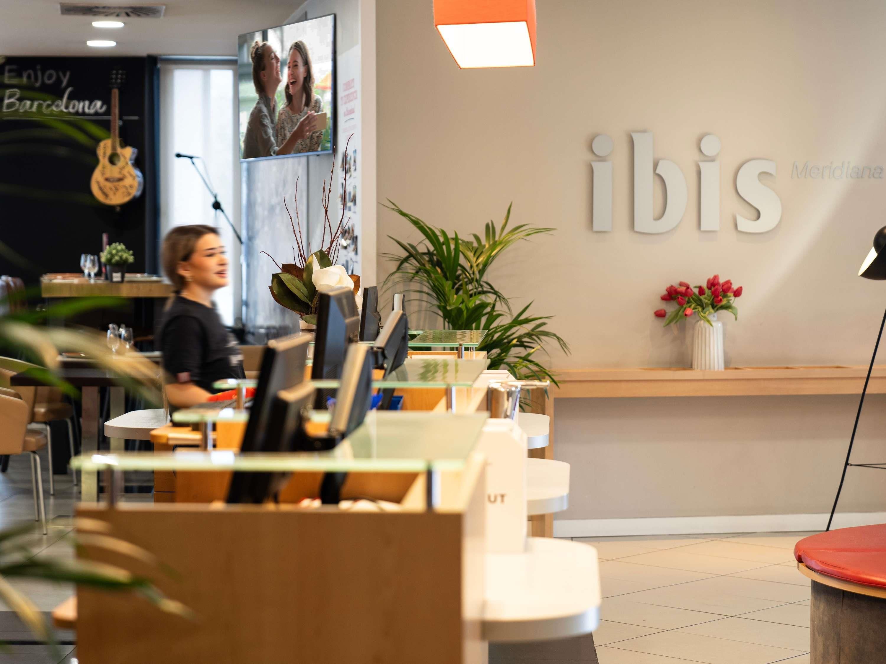 Um interior moderno com uma mesa de recepção, uma placa na parede com a inscrição "ibis" e uma decoração com uma guitarra.