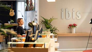 Um interior moderno com uma mesa de recepção, uma placa na parede com a inscrição "ibis" e uma decoração com uma guitarra.