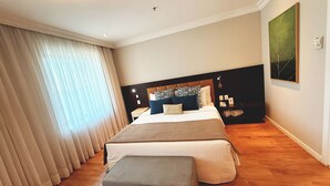 Um quarto moderno com uma cama grande, uma mesinha de cabeceira, um banquinho e uma janela com cortinas.