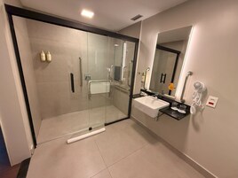 Uma casa de banho moderna com cabine de duche em vidro, uma sanita branca e um espelho.