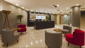 Um lobby moderno com balcão de recepção, áreas de estar e uma escadaria.