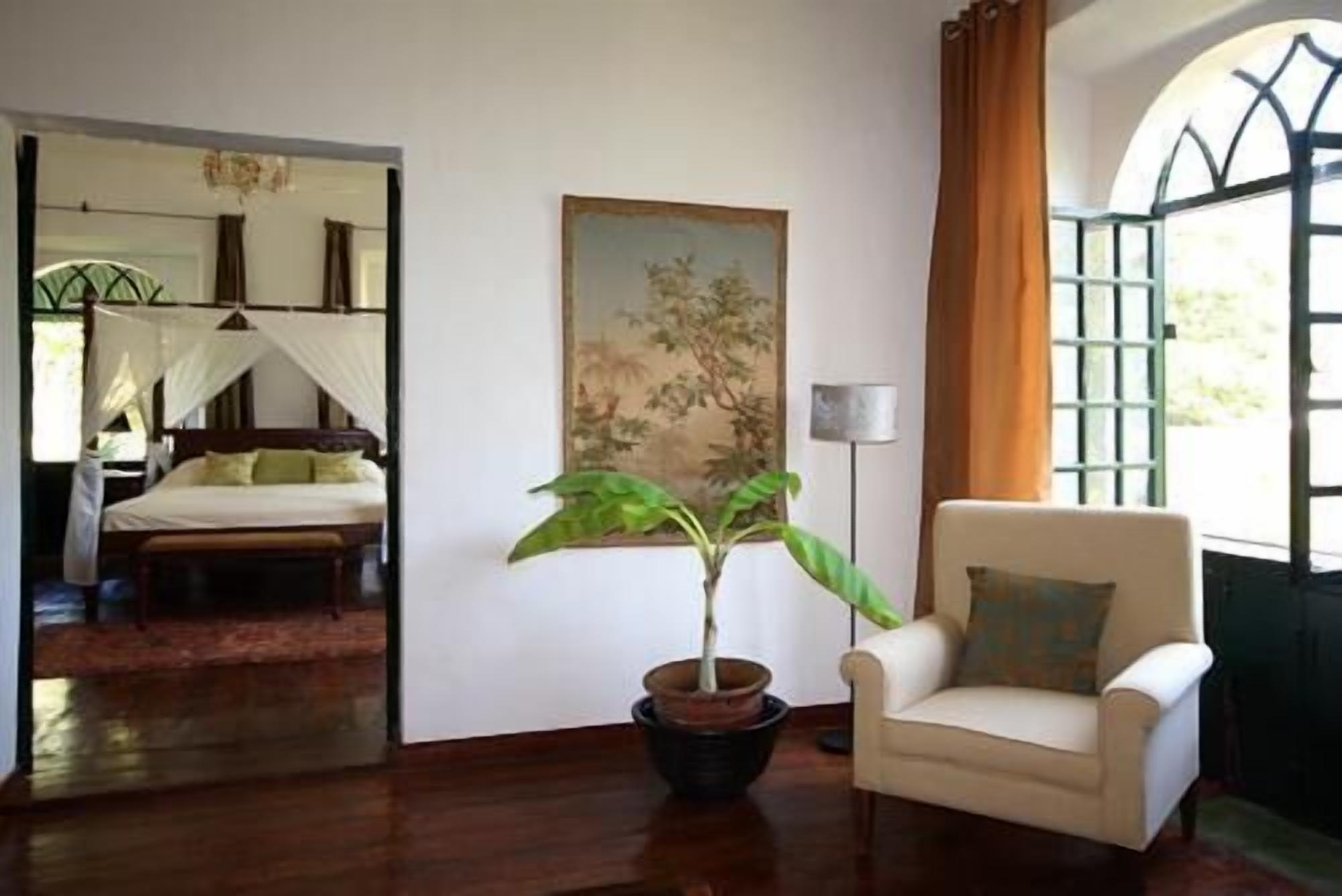 Um quarto com uma cama, uma cadeira, um vaso de planta, um quadro e uma janela com cortinas.