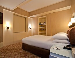 Quarto de hotel com uma cama grande, mesas de cabeceira, prateleira embutida com artigos de higiene e um espelho.