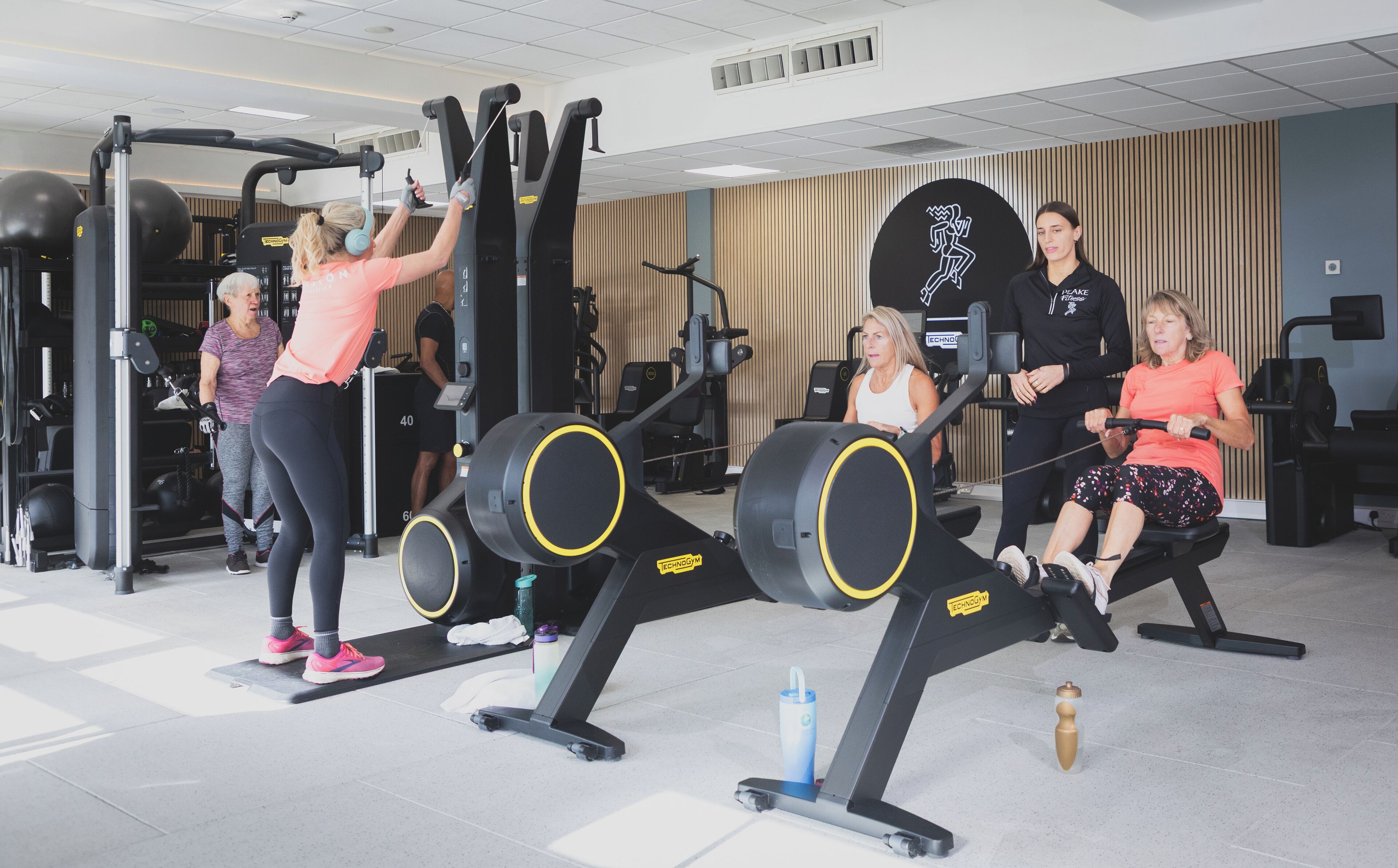 Uma academia com diversos equipamentos de exercícios, incluindo aparelho de cabo e esteiras.