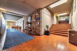 Um hall espaçoso com escada de madeira, tapete estampado em azul e parede de pedra com relógio.