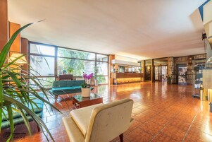 Um hall amplo com um sofá verde, uma poltrona bege e um balcão de recepção.