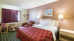 Quarto de hotel com uma cama, duas cadeiras, uma mesinha e um quadro na parede.