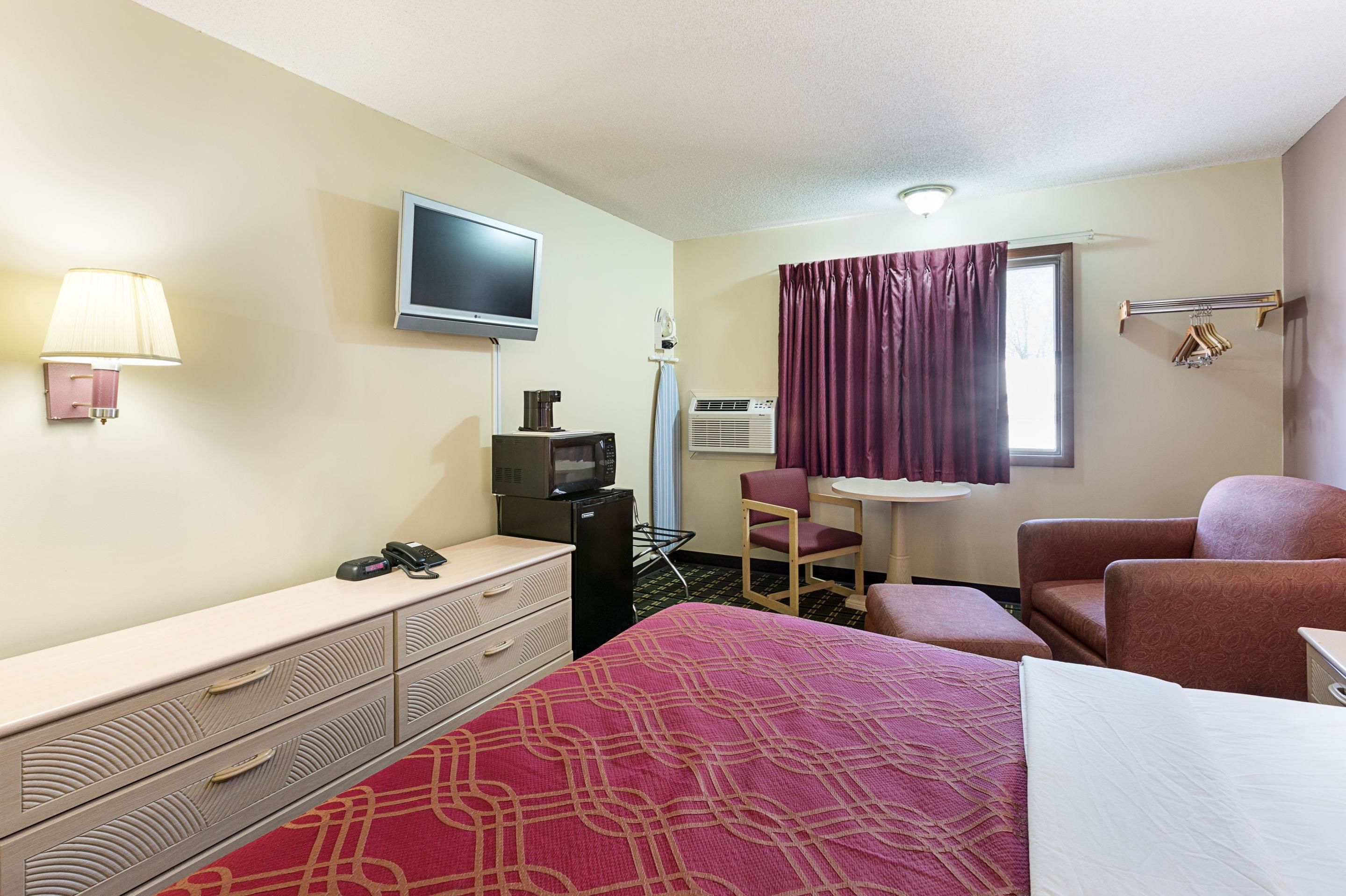 Quarto de hotel com cama, escrivaninha, cadeira, televisão, telefone e frigobar.