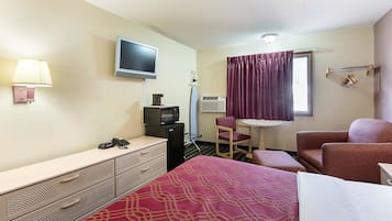 Quarto de hotel com cama, escrivaninha, cadeira, televisão, telefone e frigobar.