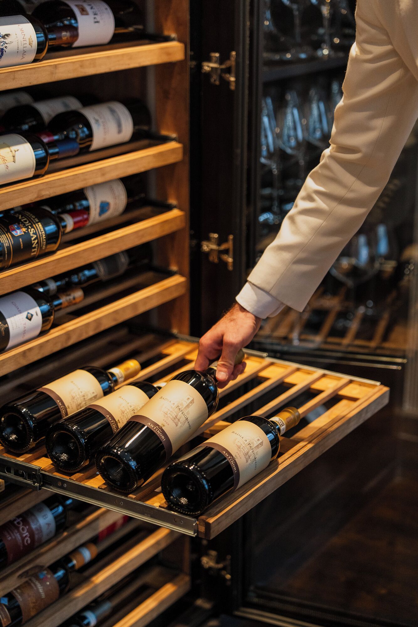 Uma mão escolhendo uma garrafa de vinho de uma estante de madeira em uma adega.