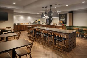 Restaurante moderno com ilha central, banquetas de bar, mesas de madeira e sofá verde.