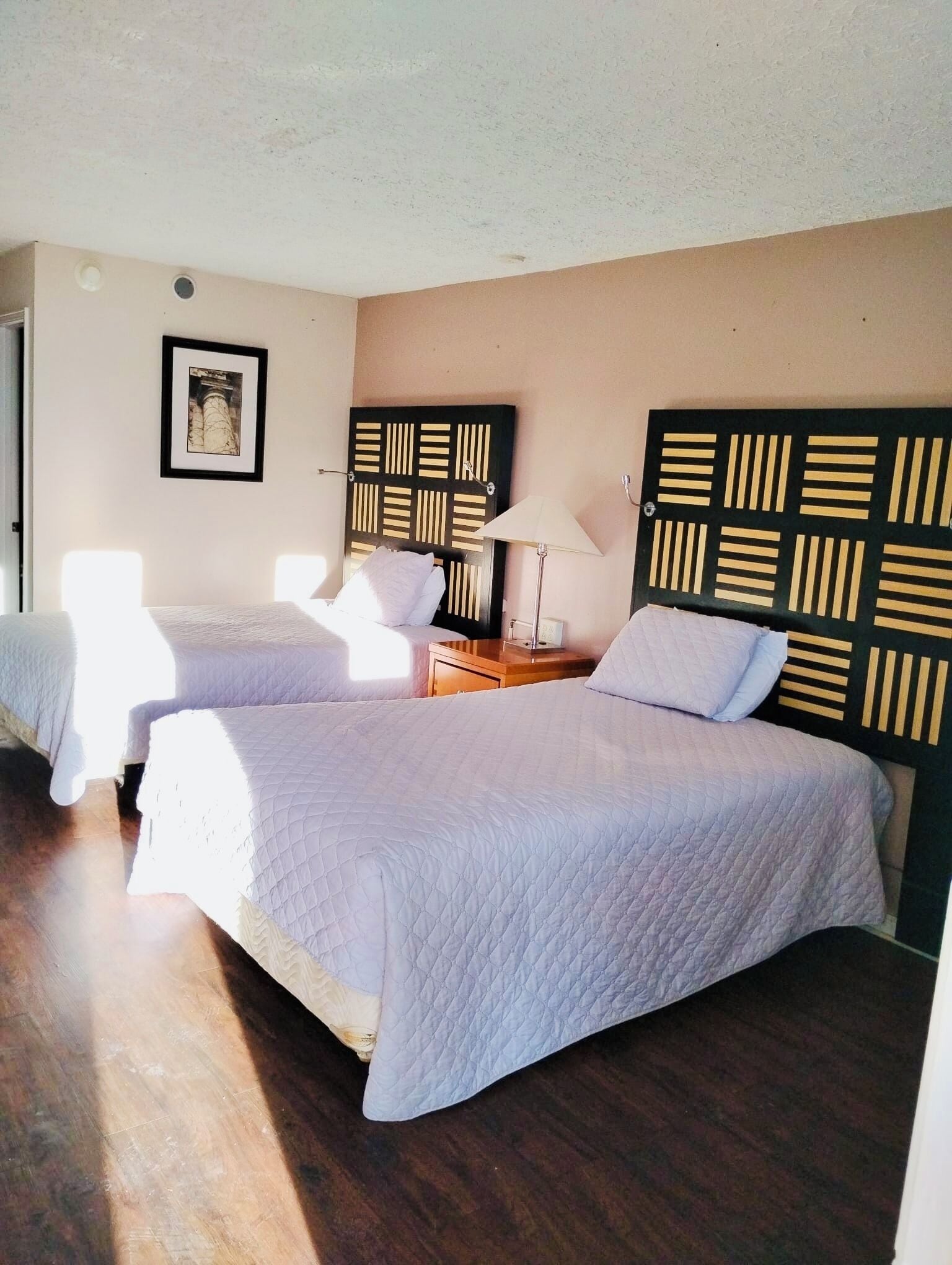 Quarto de hotel com duas camas, uma mesa de cabeceira, um abajur e um quadro na parede.