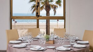 Mesa posta para refeição com vista para a praia e palmeiras através de uma janela.