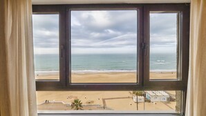 Vista da janela com vista para uma praia sob um céu claro.