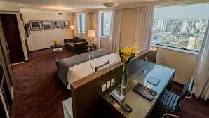 Quarto de hotel com cama, escrivaninha, cadeira e vista para a cidade.