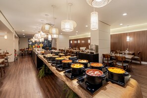 Disposição de buffet com várias estações de comida quente e áreas de estar.