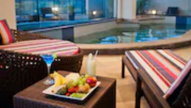 Uma área de estar moderna ao ar livre com piscina, assentos e uma cesta de frutas sobre uma mesa.