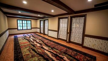 Um quarto amplo com um tapete grande estampado, vigas de madeira no teto e uma janela com cortinas padronizadas.