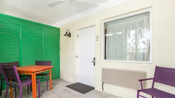 Um quarto com uma mesa e cadeiras, uma porta branca, uma janela com vista e um ventilador de teto.