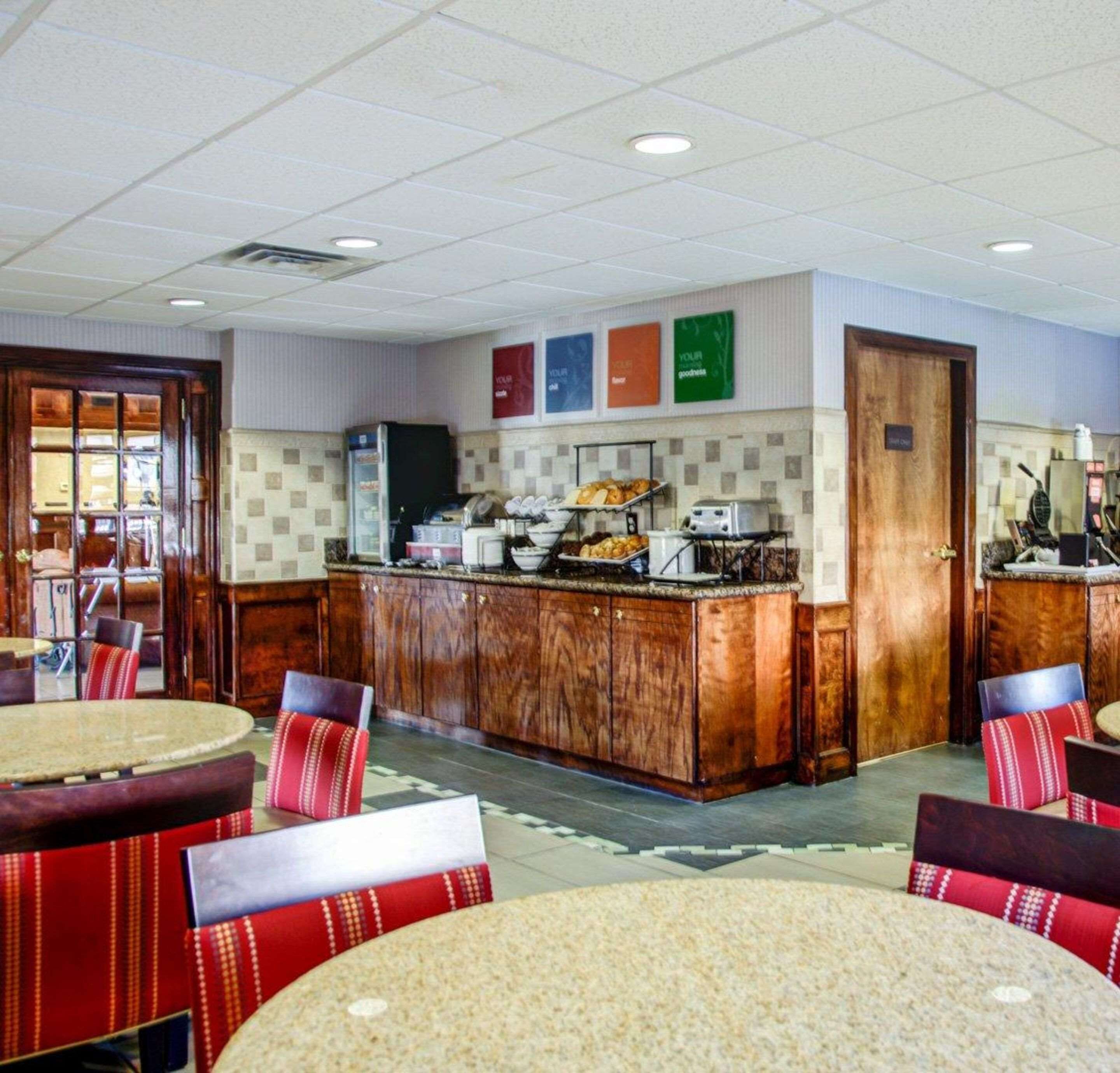 Espaço de refeições de hotel com balcão de buffet, várias mesas e cadeiras.